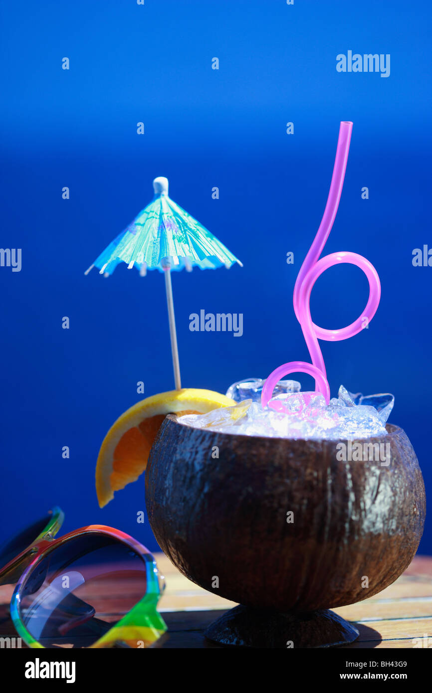 A tropical cocktail in a coconut shell and a pair of sunglasses against ...