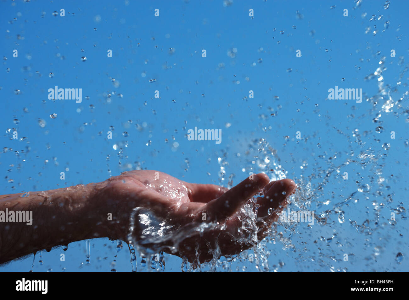 Droplets of water falling on to the palm of a man's hand against a blue ...