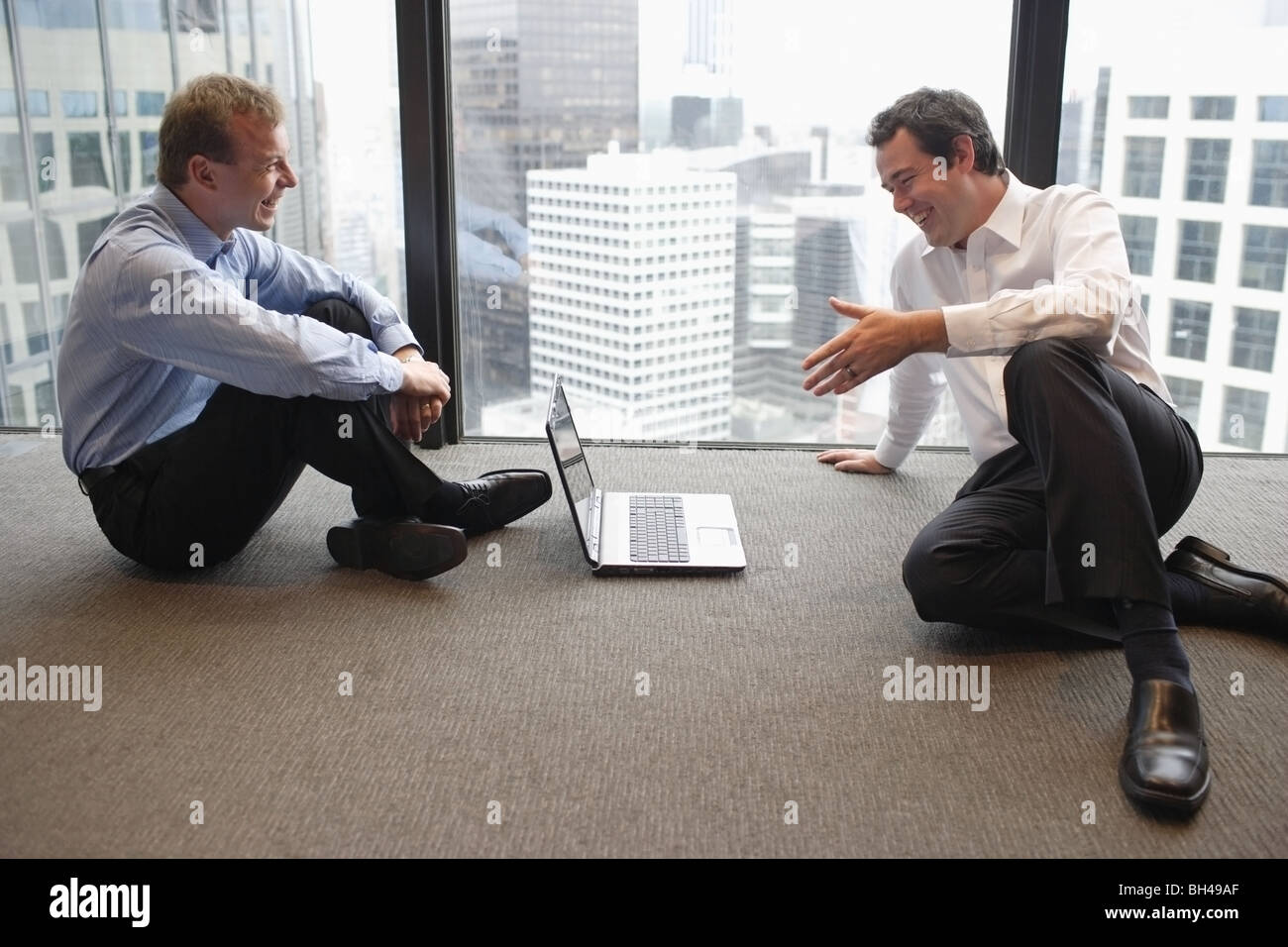Two businessmen sitting on the office floor with a laptop computer ...