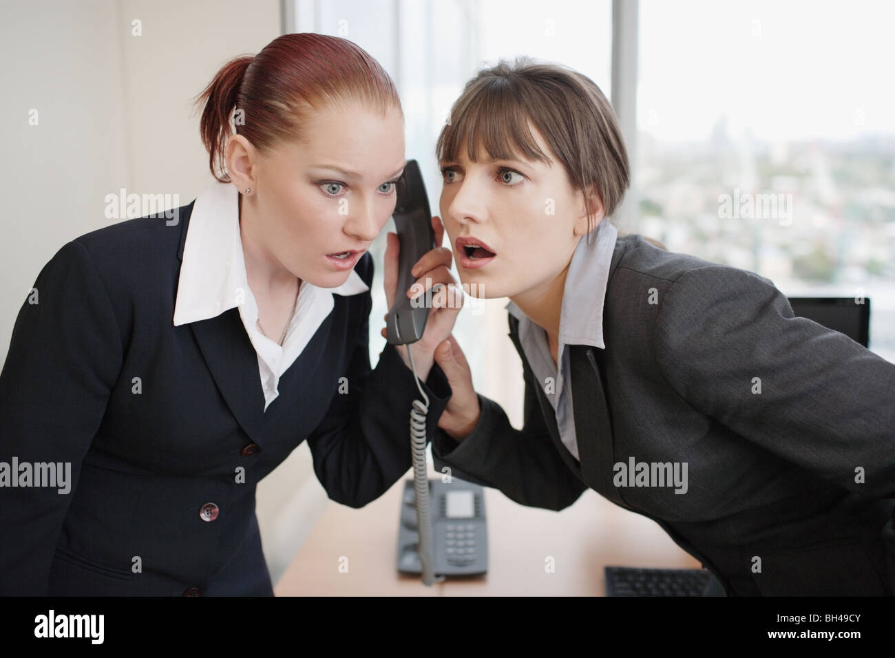 Two female office workers listening in on a telephone conversation ...