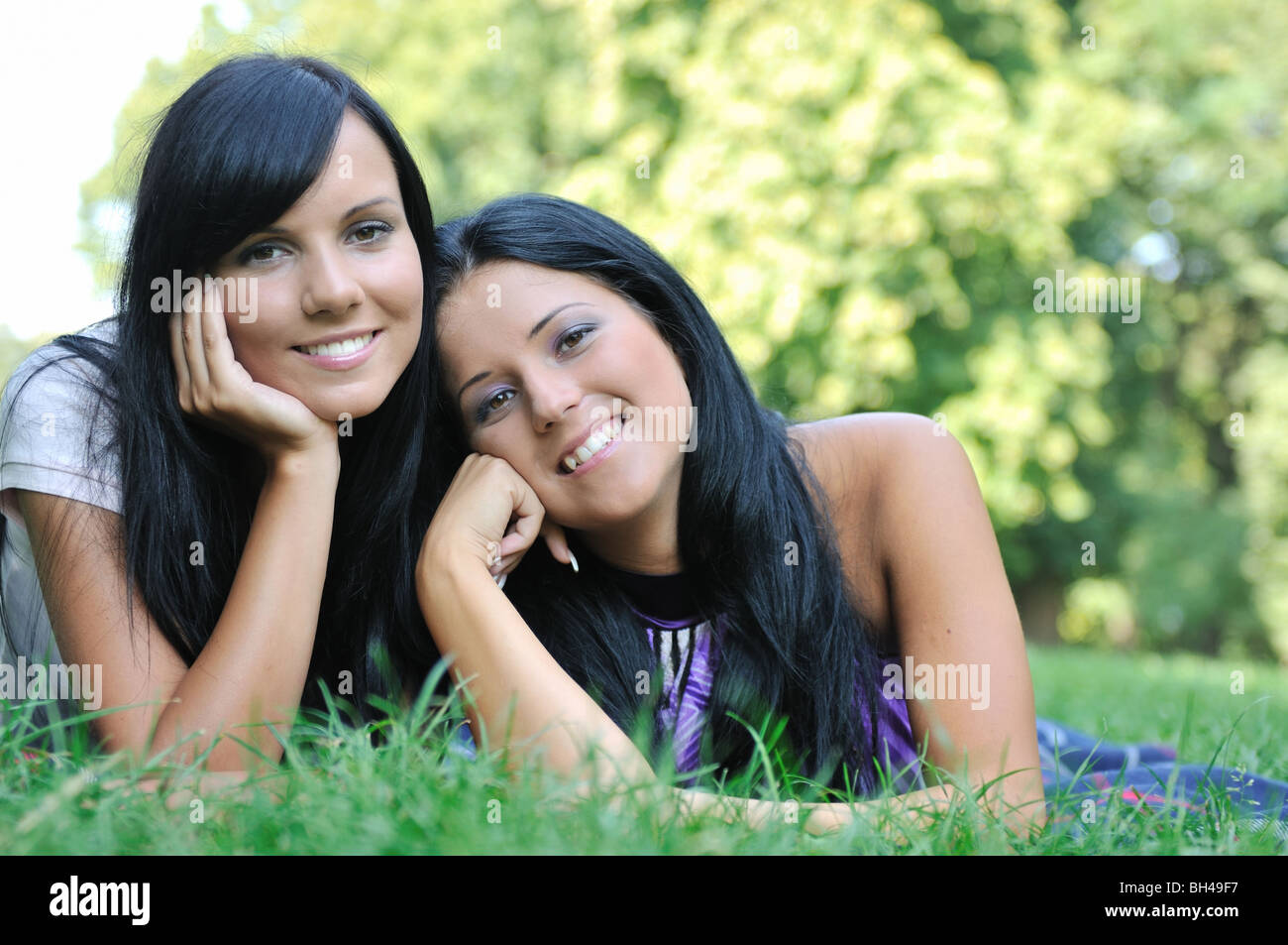 Frendship - two smiling happy sisters lying together in grass outdoors ...