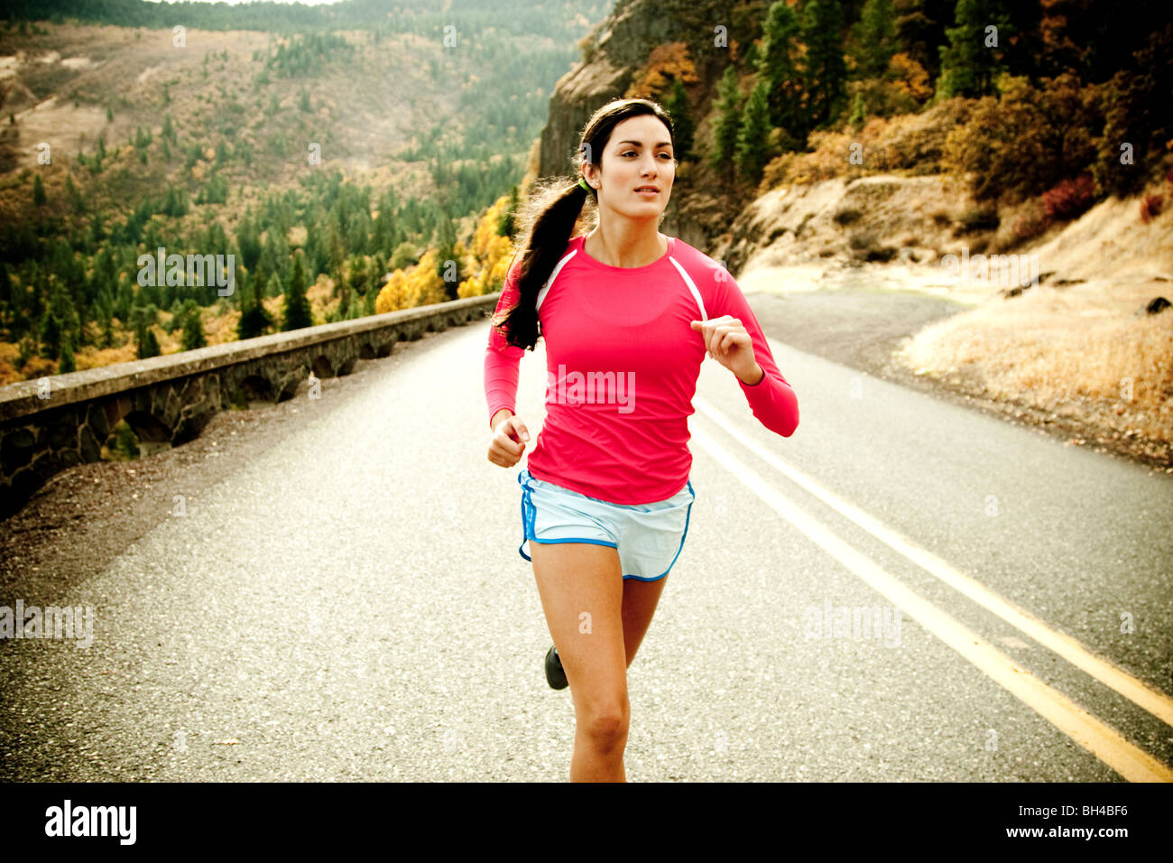 An athletic woman jogging along a deserted road on a beautiful fall day ...