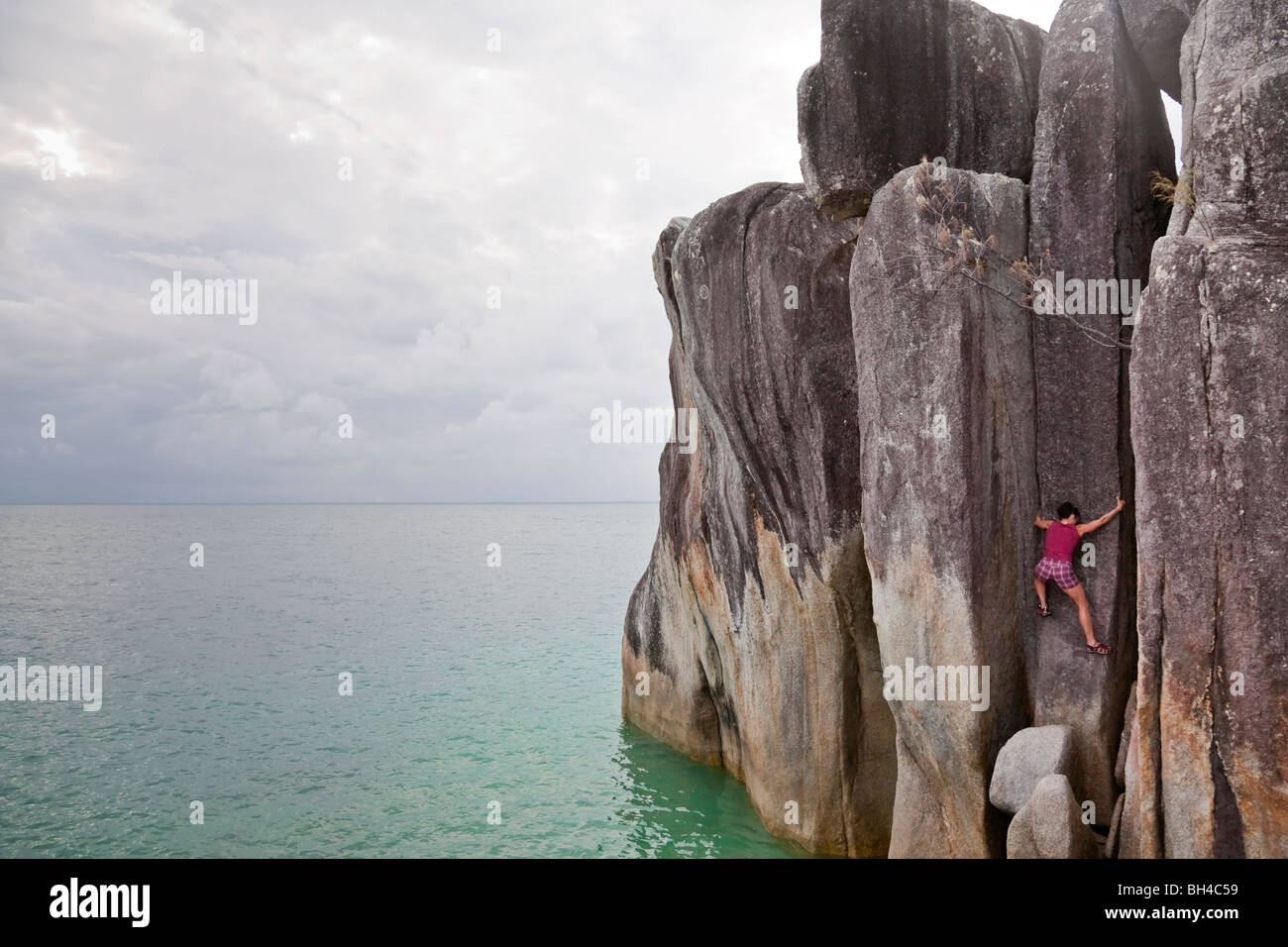 A woman climbs a granite rock pillar over the ocean on Coombe Island ...