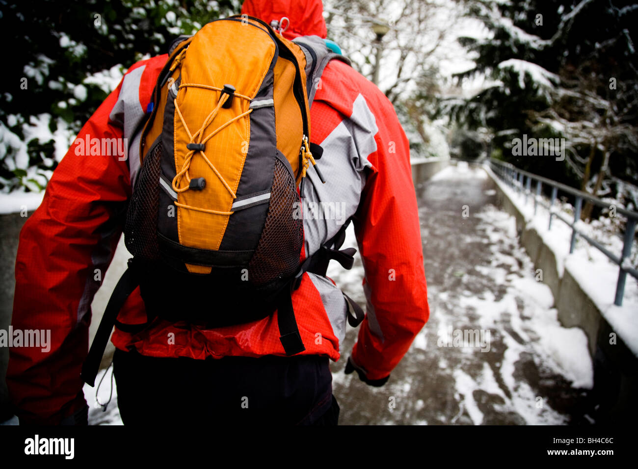 A male runner with a backpack trains on a snowy, winter sidewalk in the ...