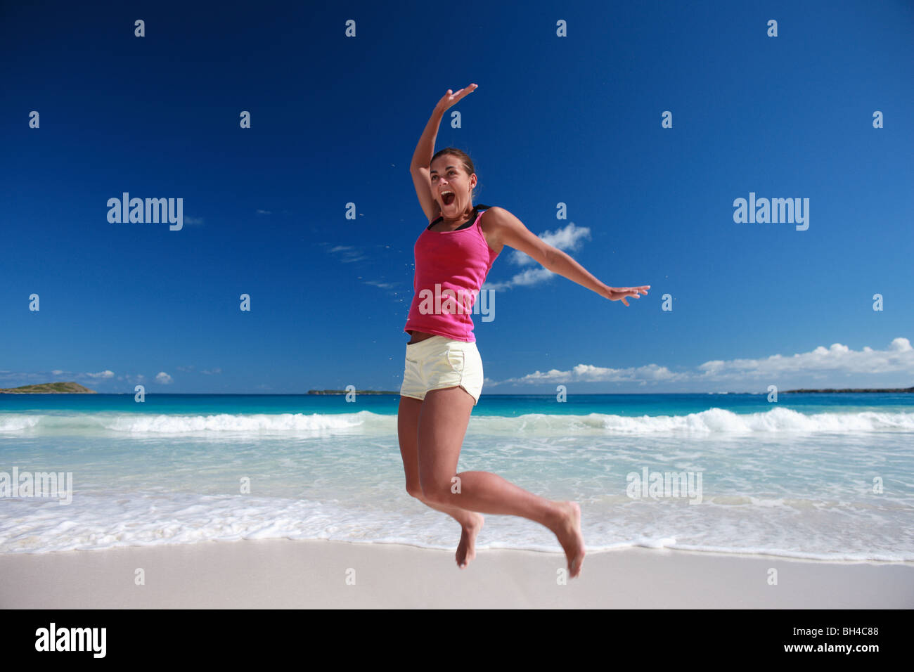 Young woman leaping in the air on a deserted tropical beach, smiling ...