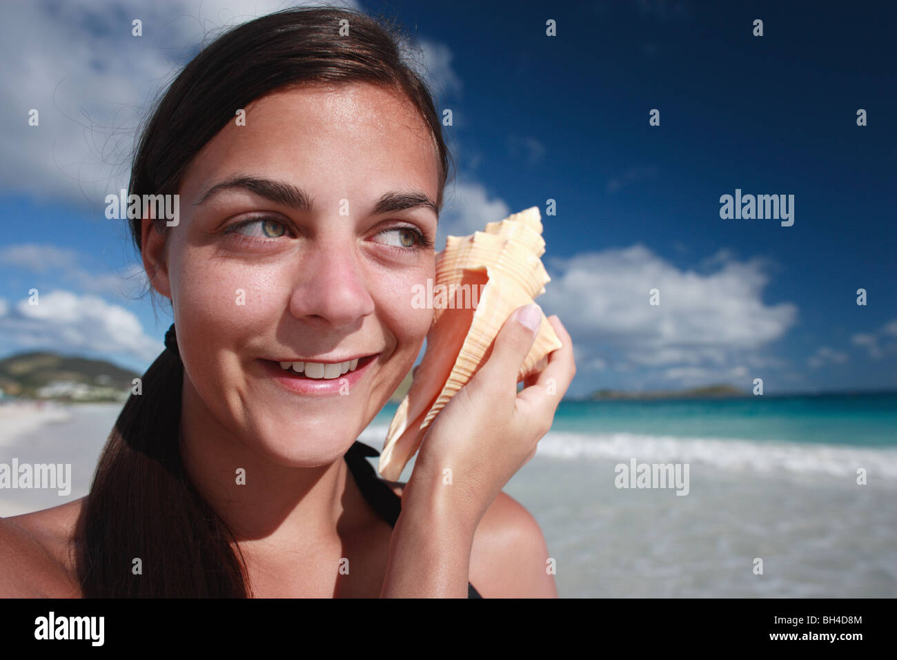 Young woman listening to the sound of a seashell on a deserted tropical ...