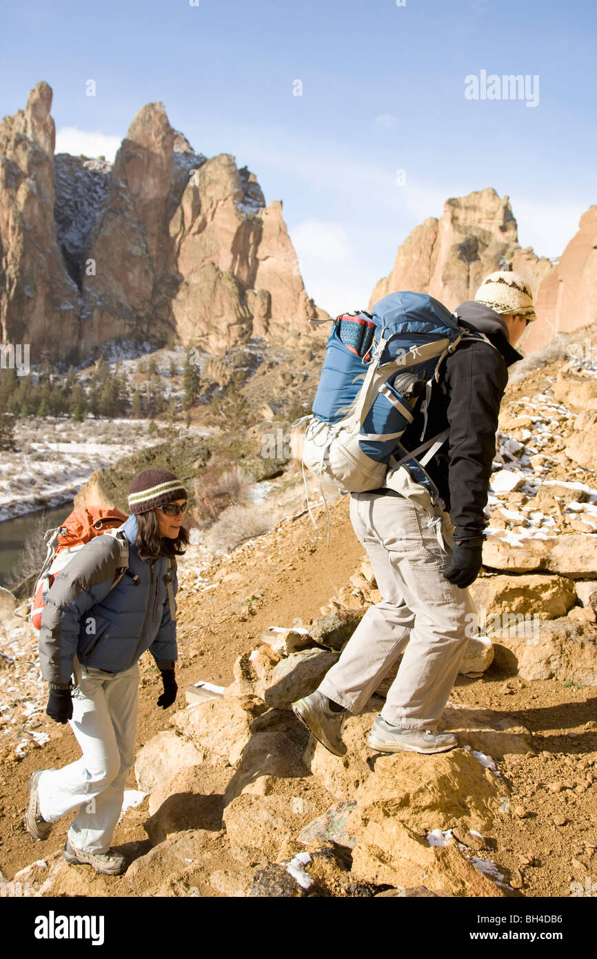 Two rock climbers with backpacks walking down a trail with a cliff in ...