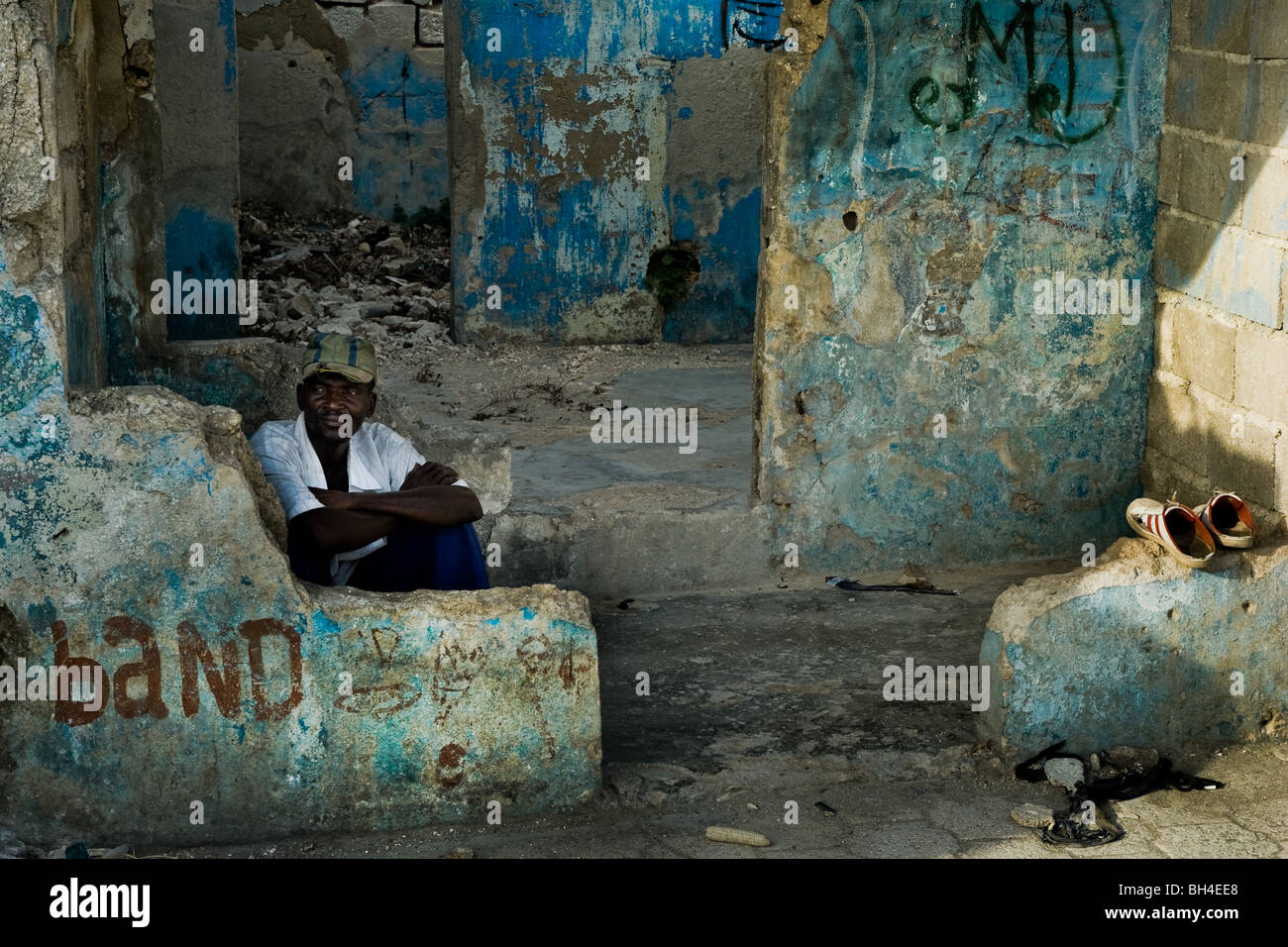 A Haitian man resting in a shadow inside a house ruin in the slum of ...