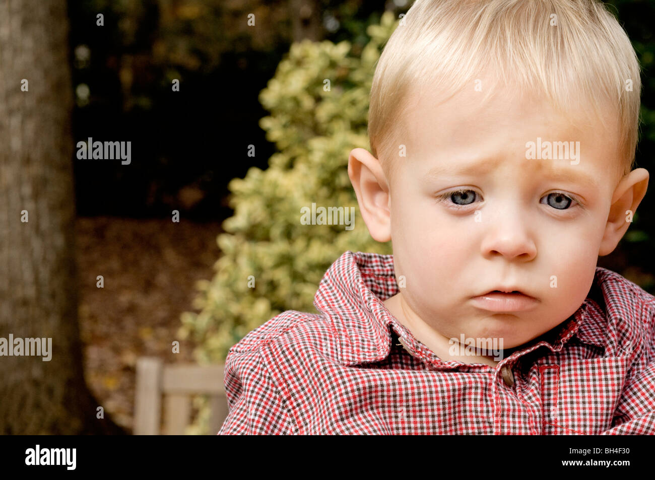 Little boy frowning sitting outdoors Stock Photo - Alamy