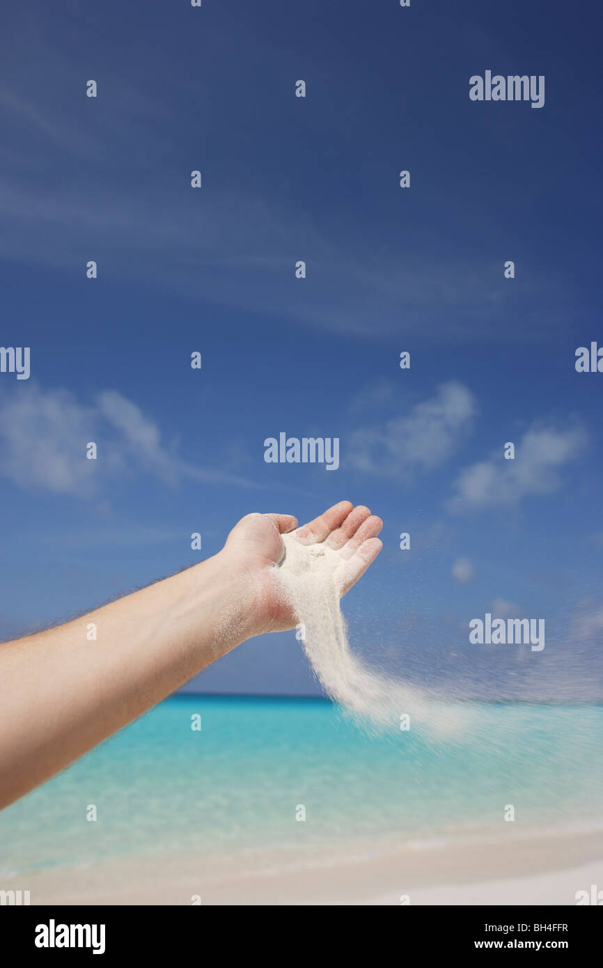 A man's hand pouring sand caught in the breeze on a deserted tropical ...