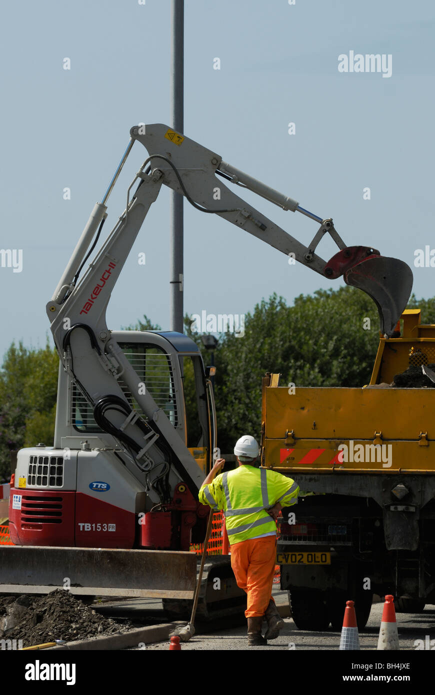 Construction workers digging up a pavement with a tracked excavating ...