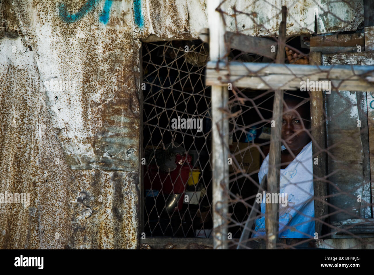 A Haitian woman looking through the wired window in the slum of Cité ...
