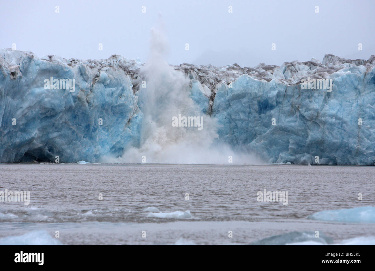Glacier of blue ice calving into the ocean creating a huge splash and following wave Stock Photo ...