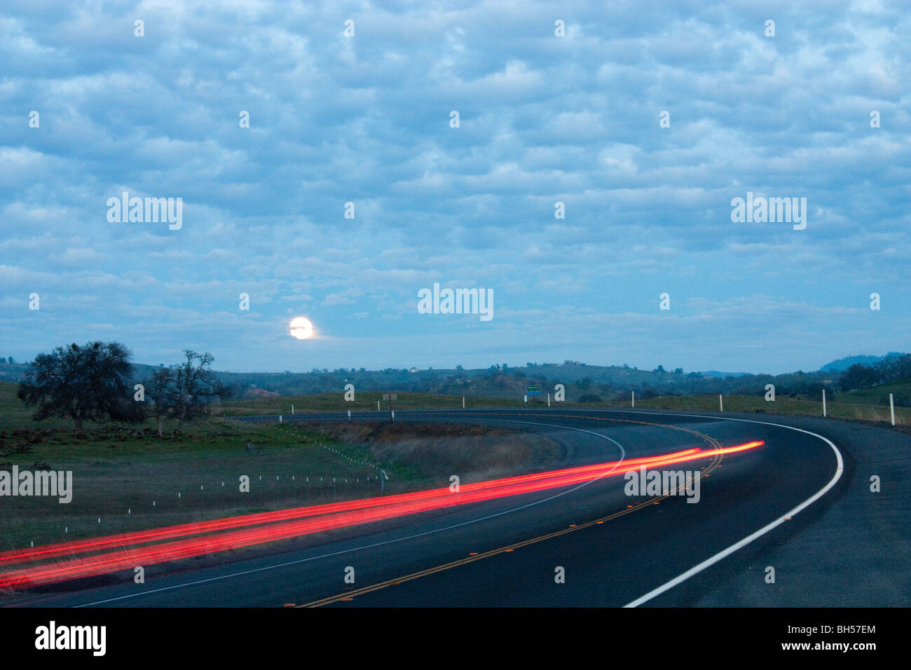 A road at night with the moon rising and headlight and tail light ...