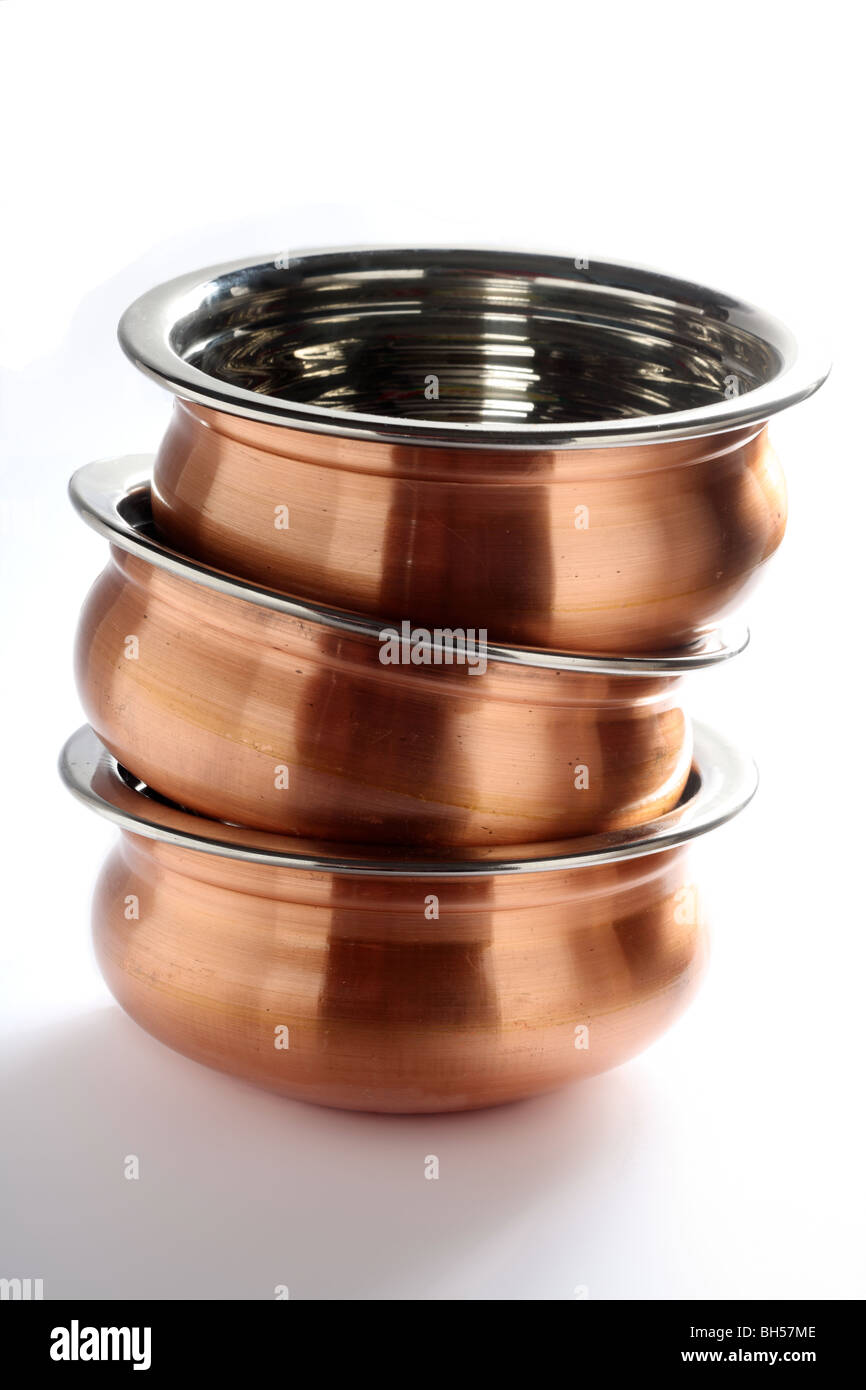 Indian copper-plated, stainless steel food pots against a white ...