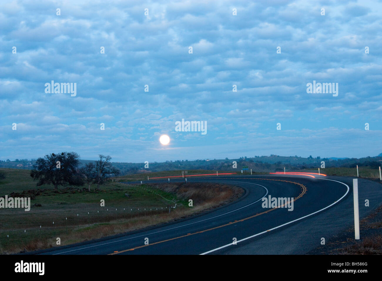 A road at night with the moon rising and headlight and tail light ...