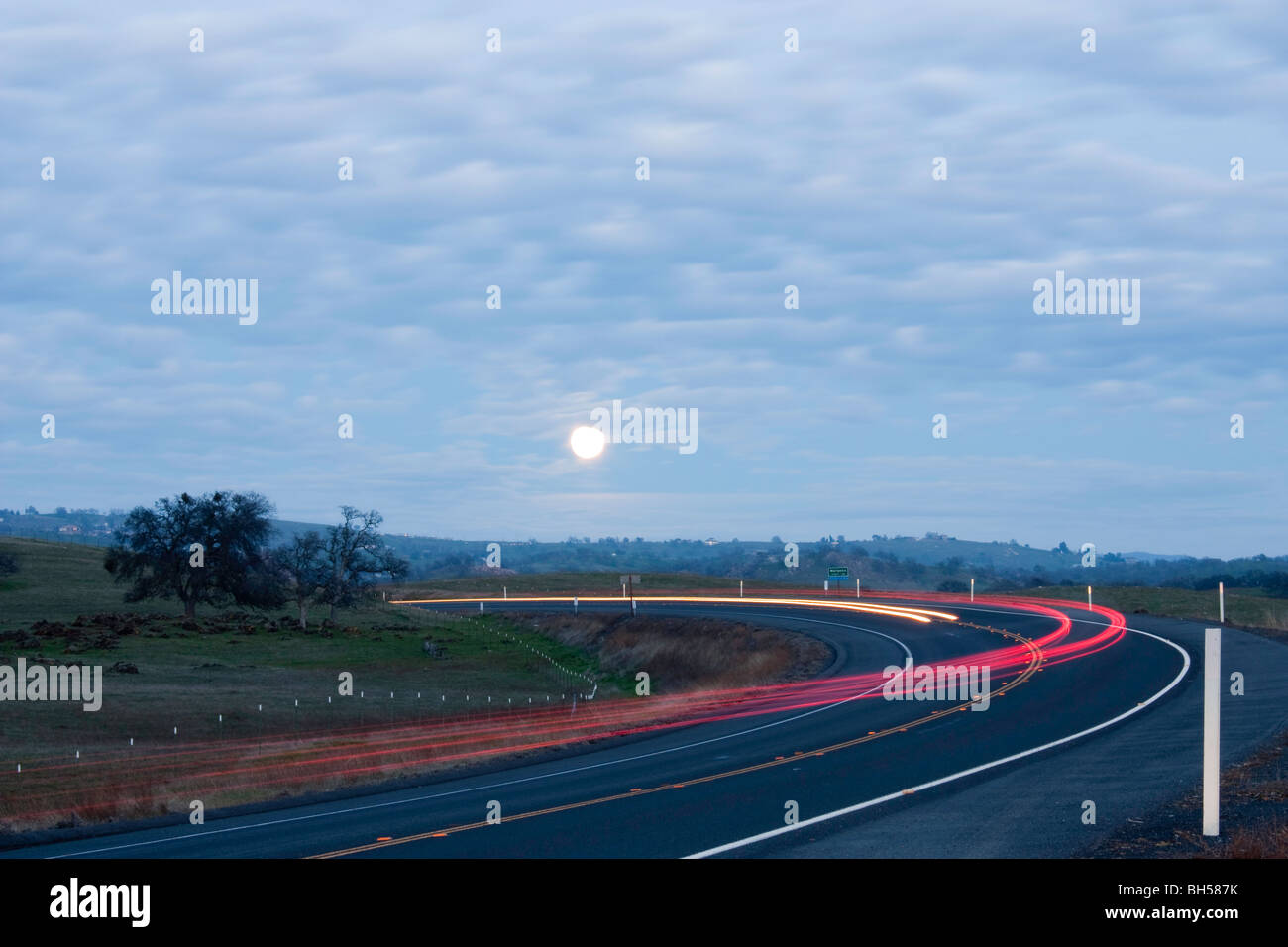 A road at night with the moon rising and headlight and tail light ...
