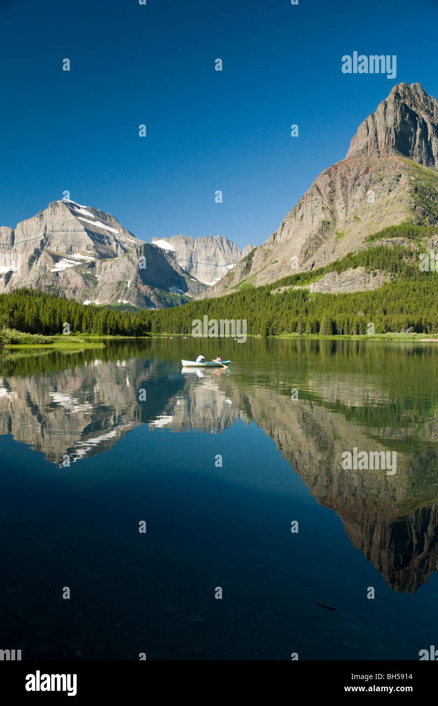 A couple rows a boat on Swiftcurrent Lake at Many Glacier with Mt ...