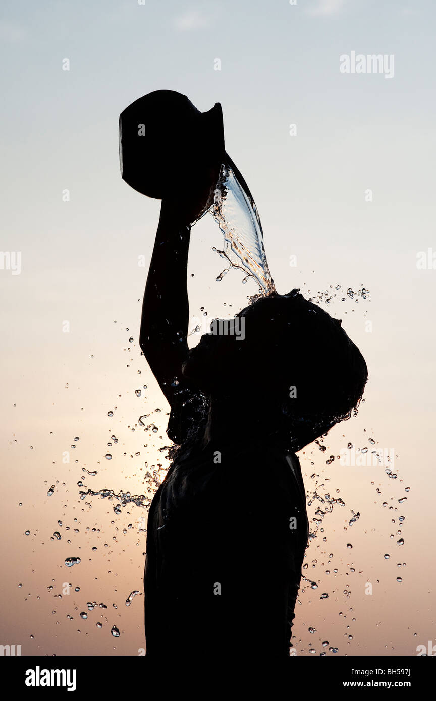 Indian boy pouring water on himself from a clay pot silhouette. Andhra ...