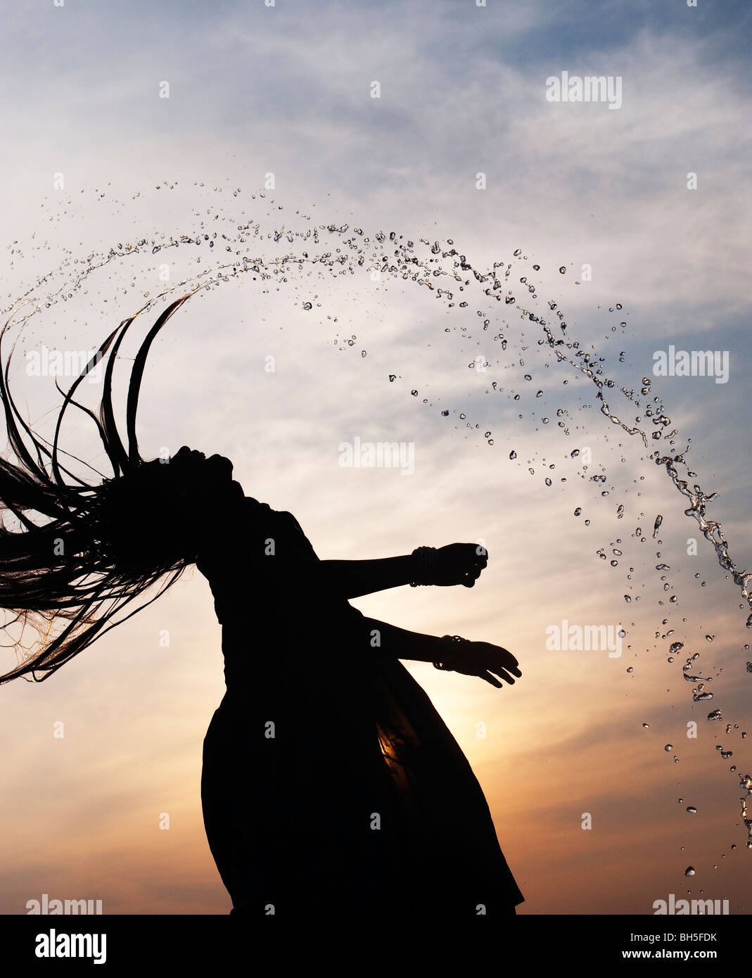 Indian girl throwing her wet hair back causing water spray silhouette ...