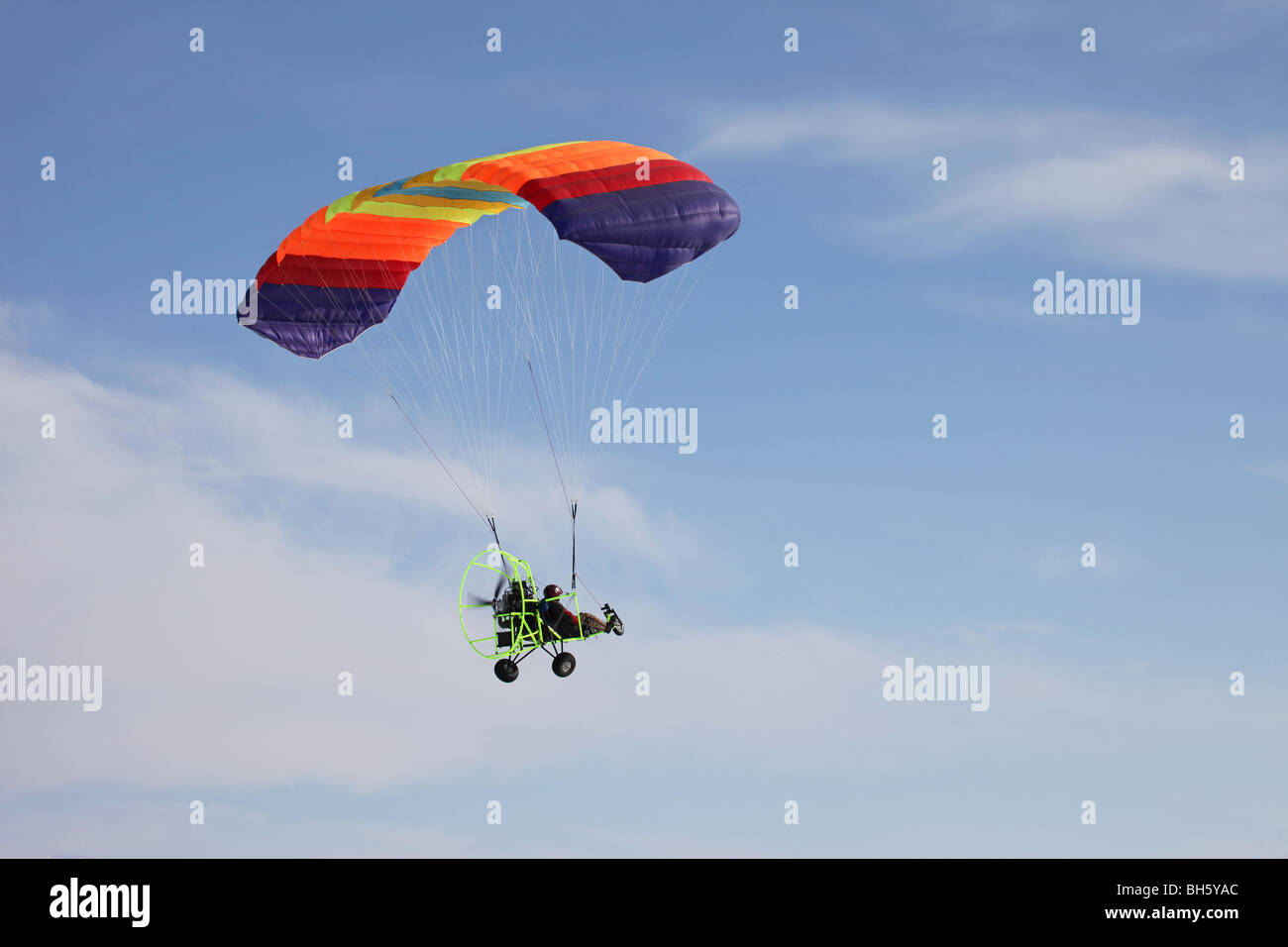 Powered parachute flying in light blue sky and clouds. Multi colored ...