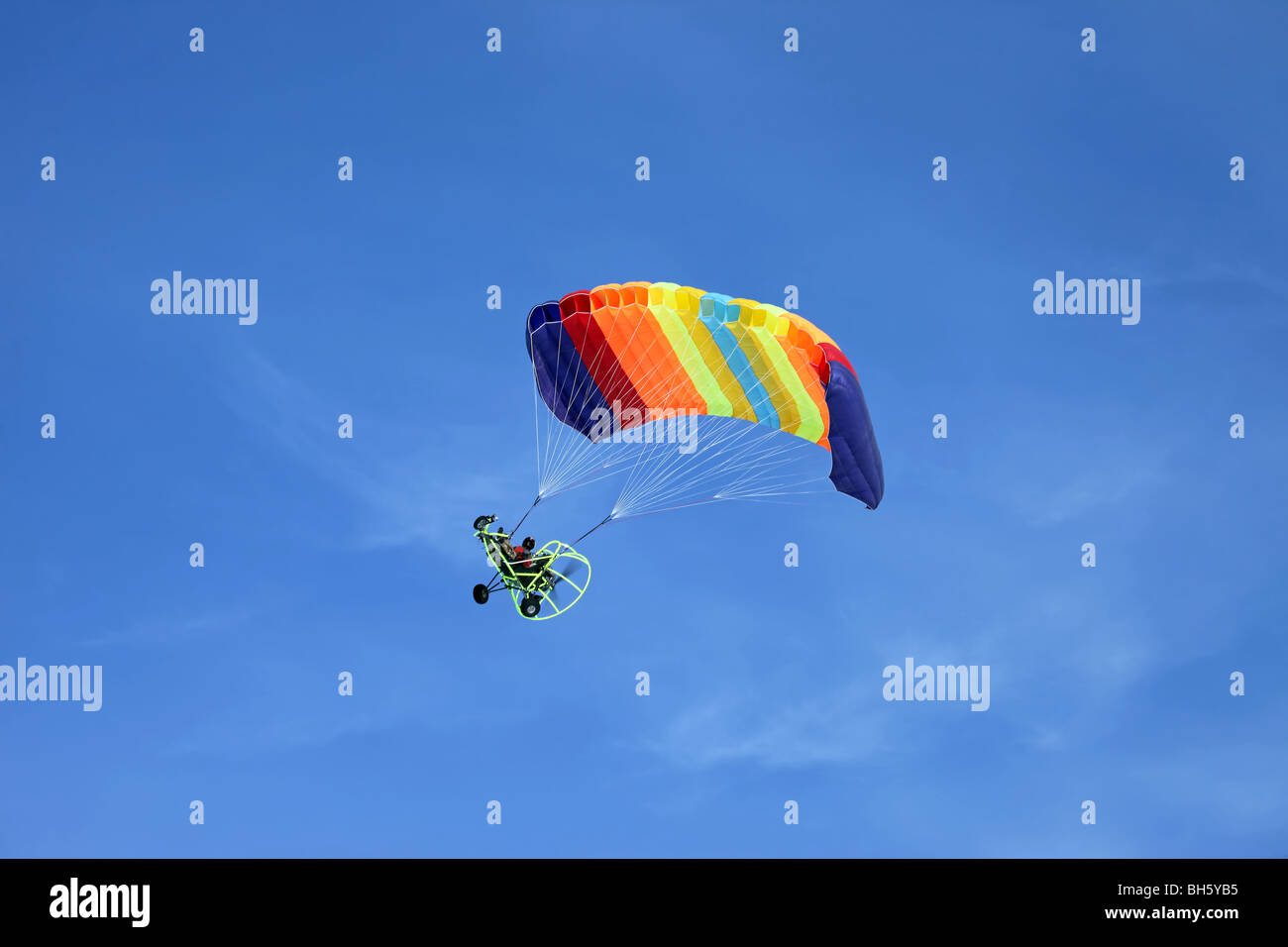Powered parachute flying above in brilliant light blue sky. Multi ...