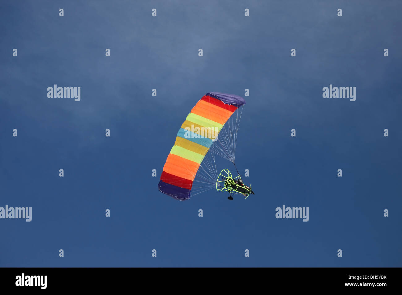 Powered parachute flying above in brilliant blue sky. Multi colored ...