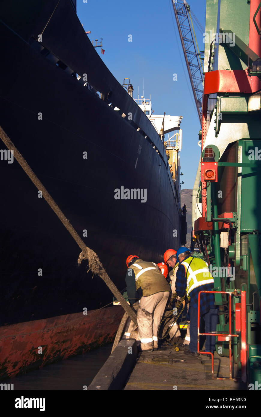 Stevedores assist in handling mooring ropes during the arrival of a ...