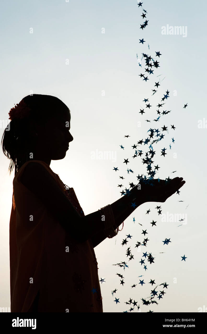 Silhouette of a young Indian girl catching falling stars at sunset ...