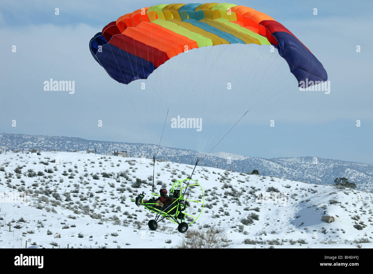 Powered parachute flying over winter snow hills. Multi colored ...
