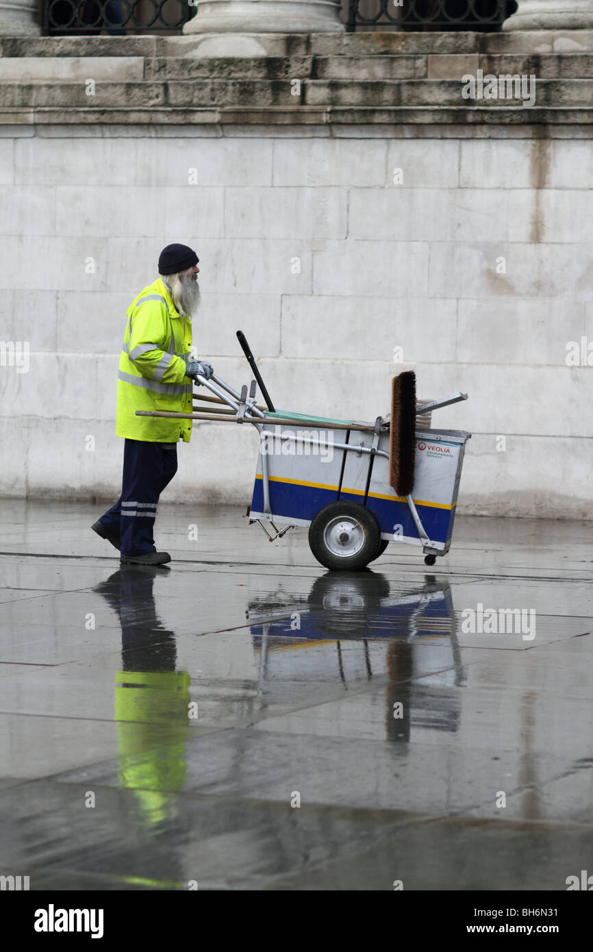A street cleaner pushes his cart in Trafalgar Square, London, along a ...