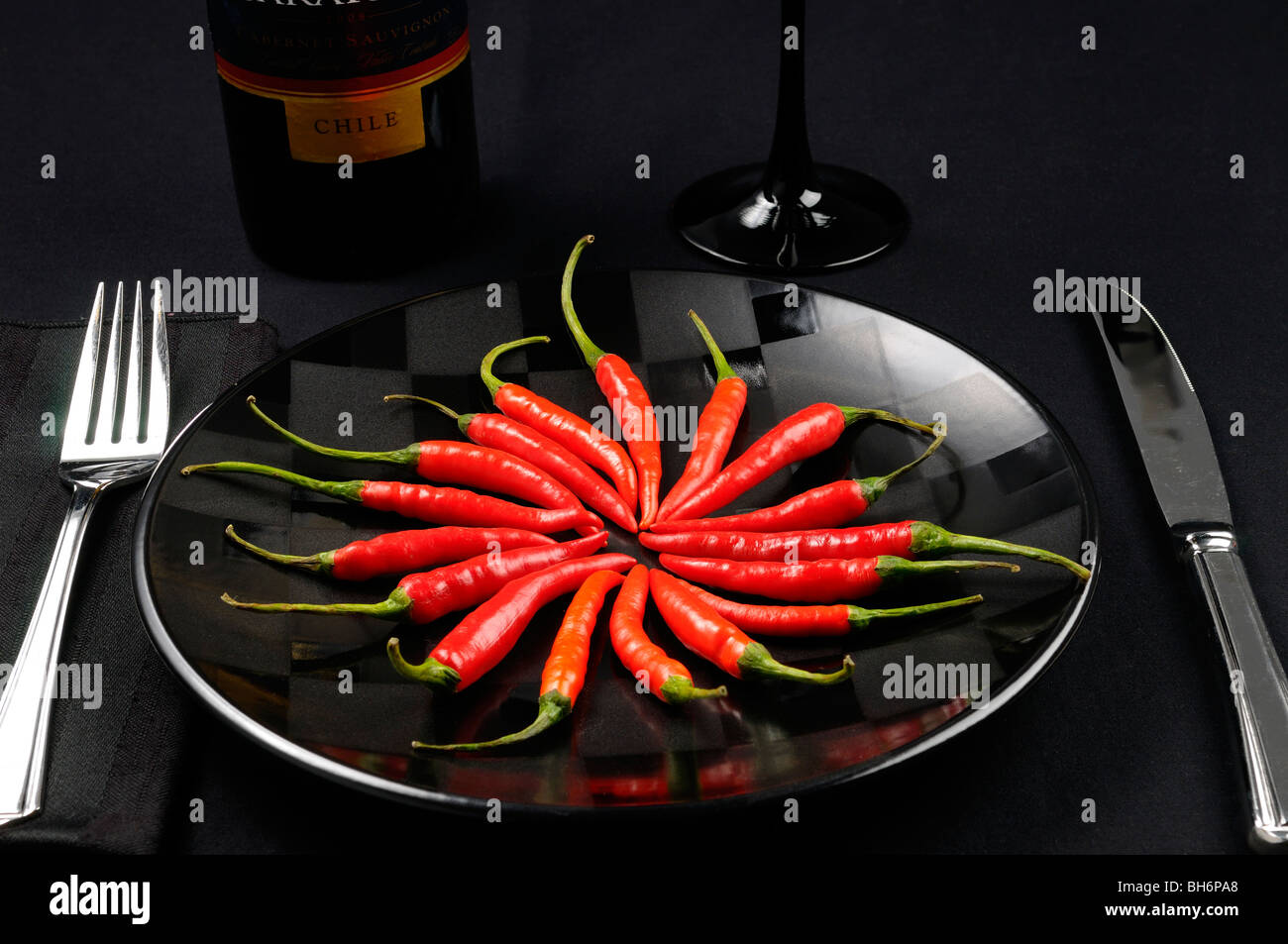 Ring of red hot Chili Peppers on a black plate table setting with wine ...
