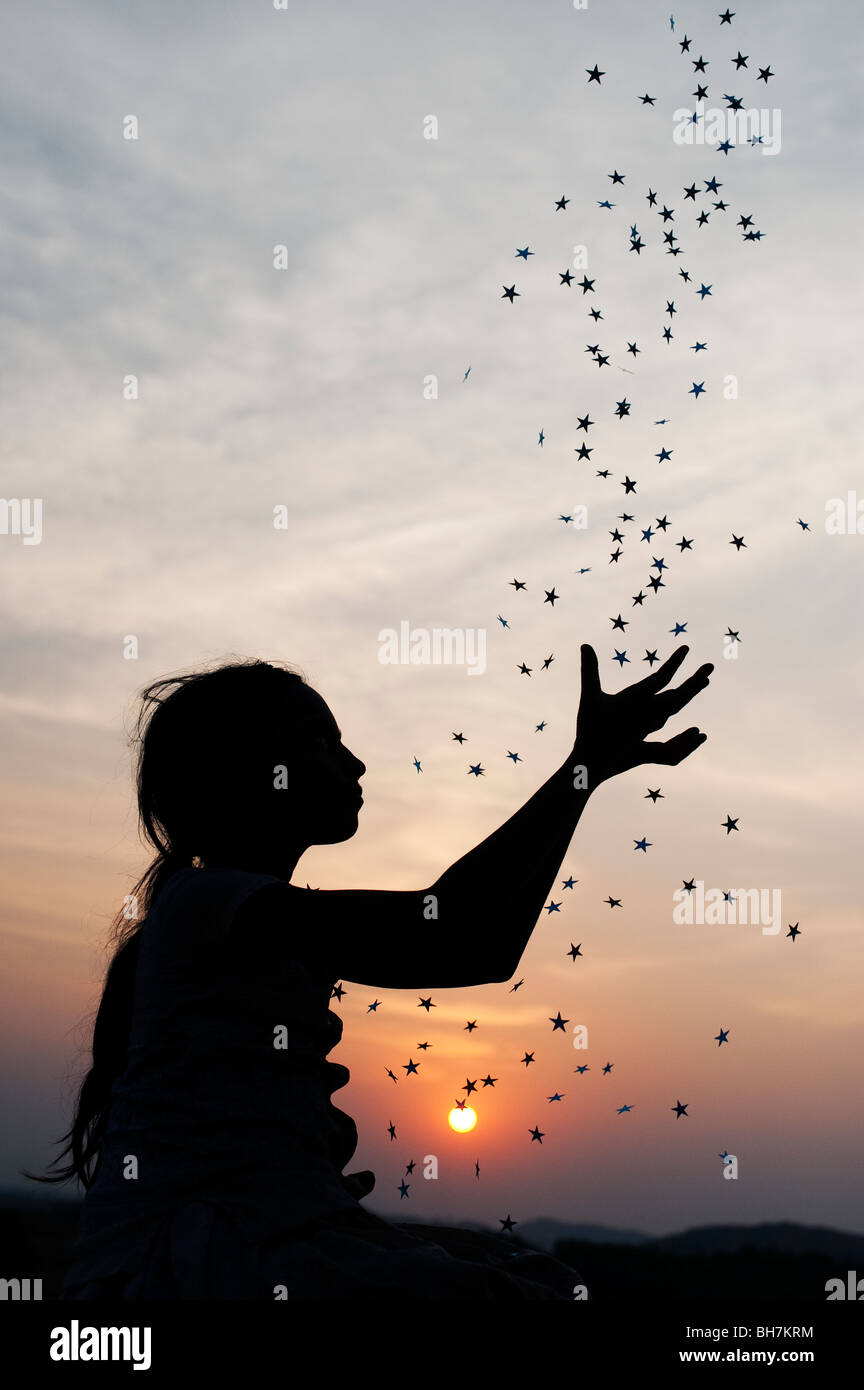 Silhouette of a young Indian girl catching falling stars at sunset ...