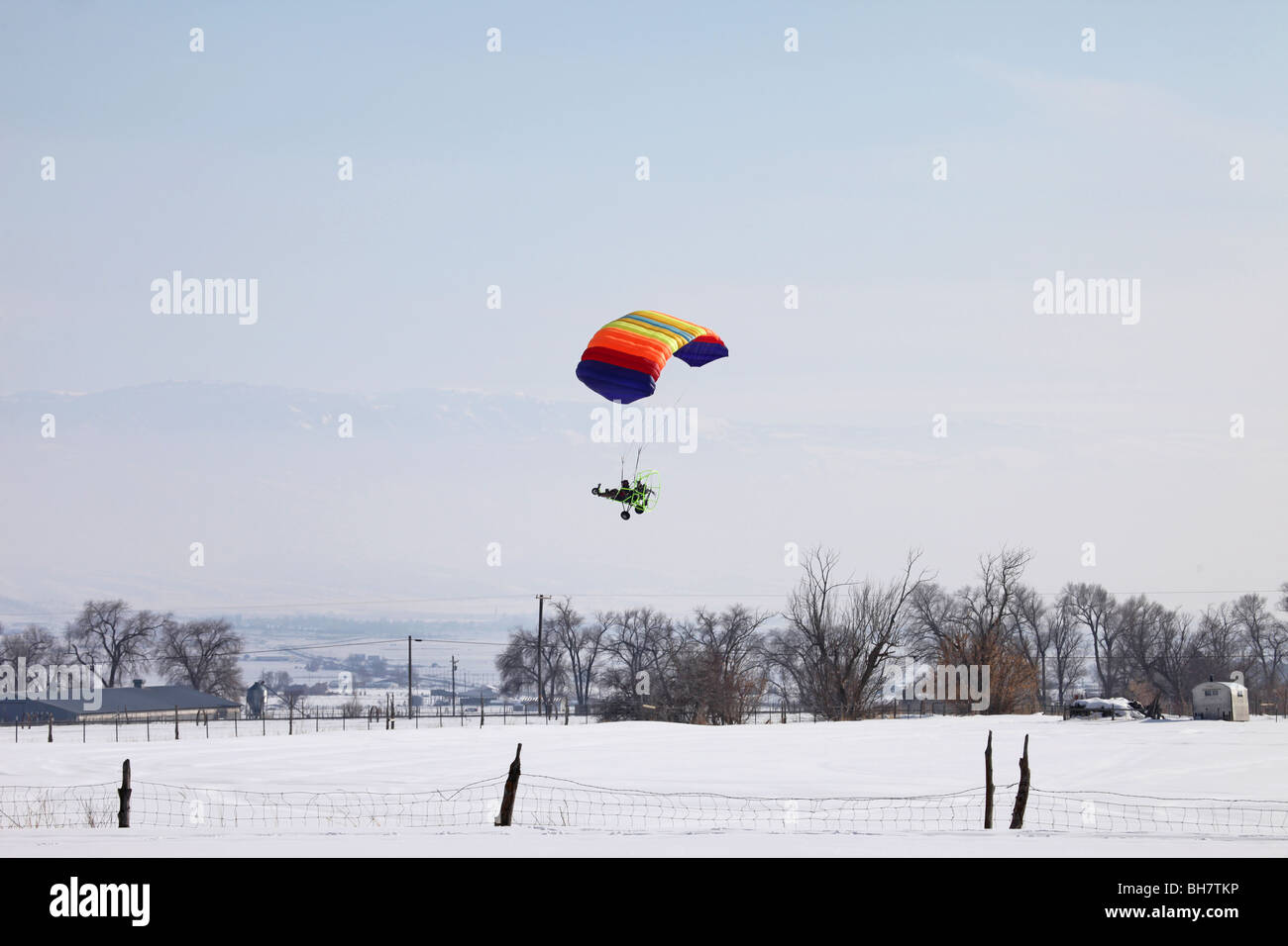 Powered parachute flying across ice and snow covered rural farms in ...