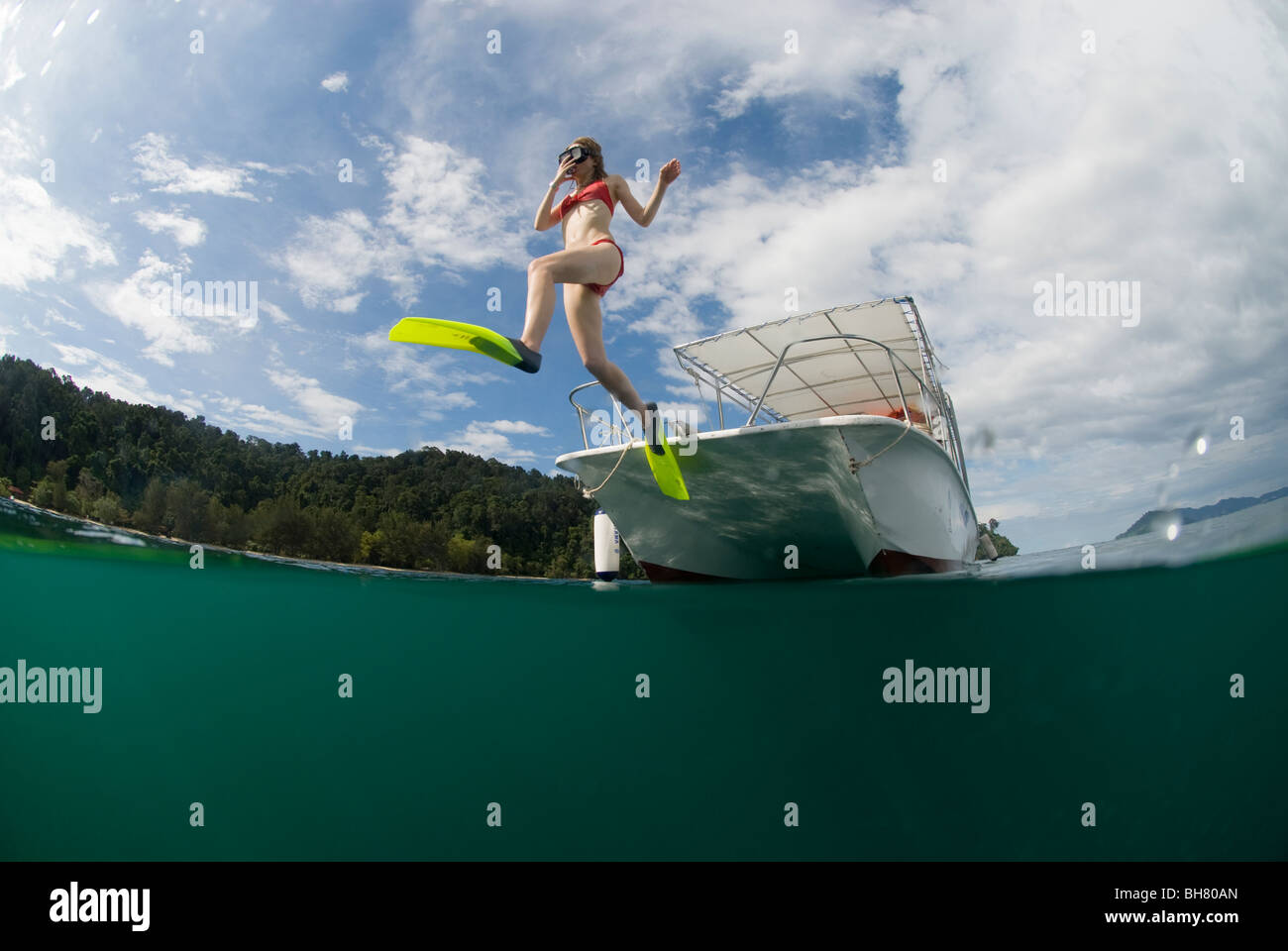 Young woman using giant stride from boat to enter water to snorkel ...
