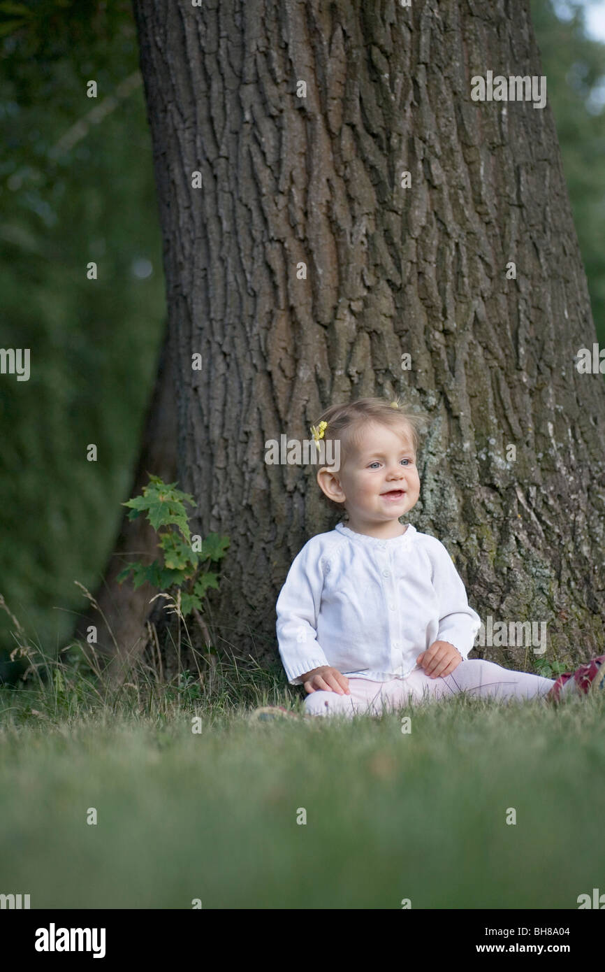A baby girl sitting under a tree and looking away Stock Photo - Alamy