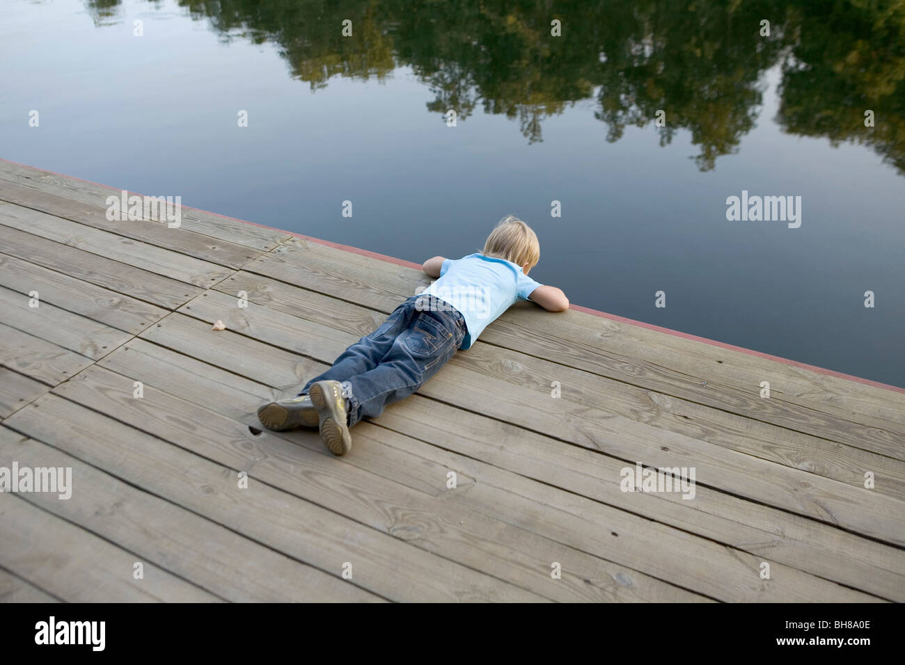 A boy looking into the water from a wooden jetty Stock Photo - Alamy