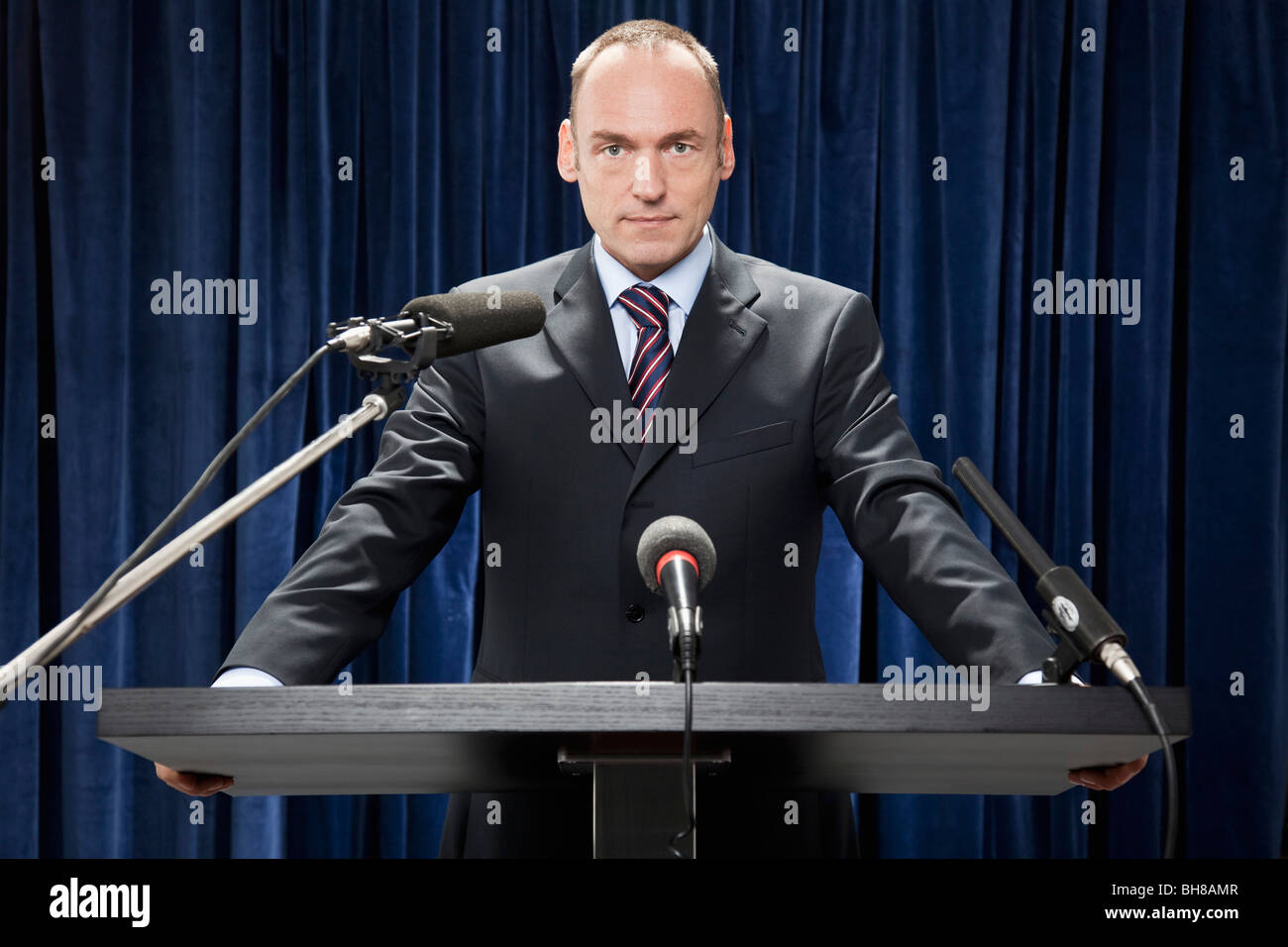 A man in a suit standing at a lectern Stock Photo - Alamy