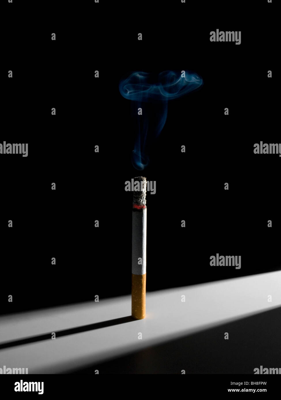 A single smoking cigarette standing in a narrow corridor of light. A ...