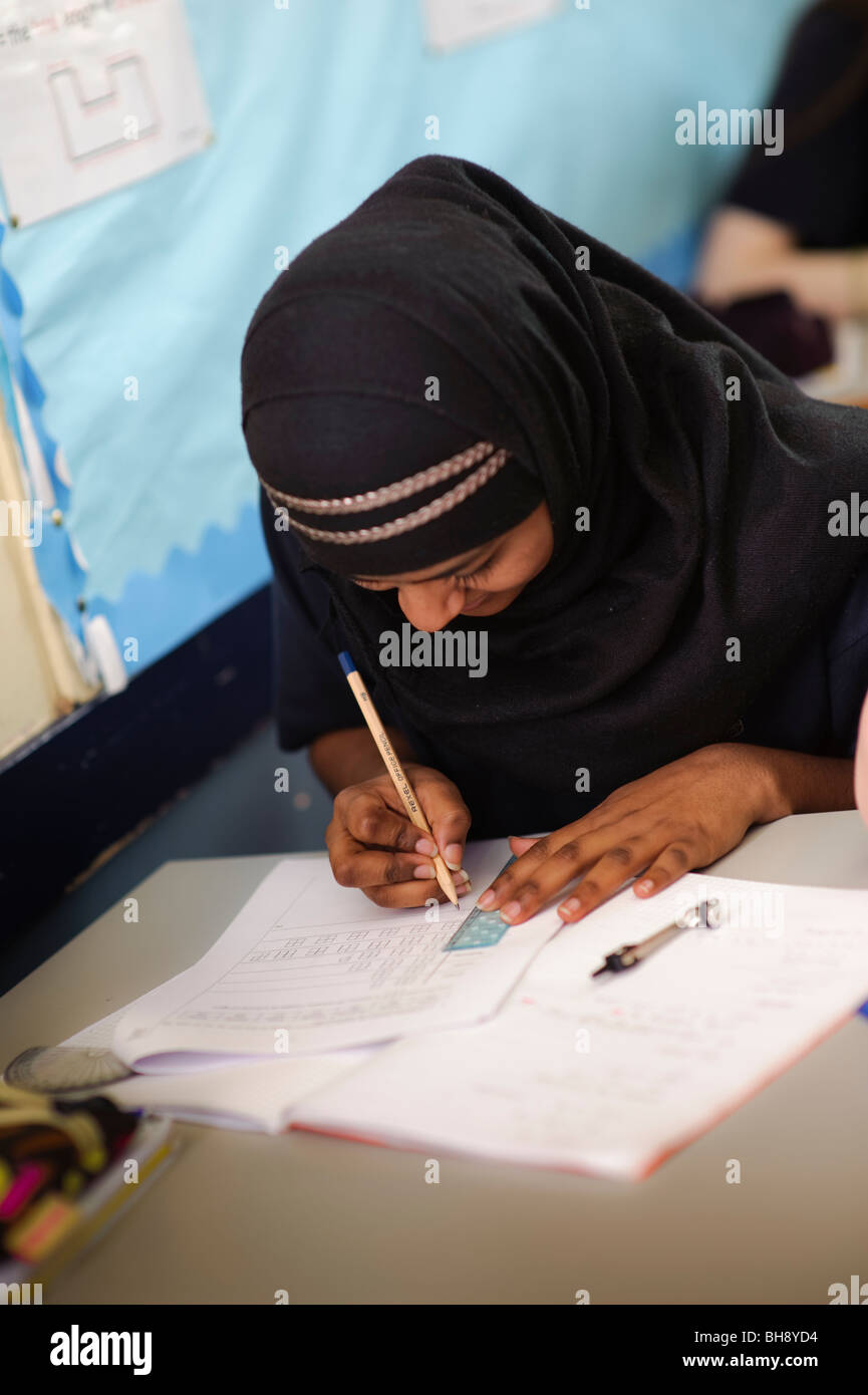 Teenage British Muslim schoolgirl writing in her notebook in a ...