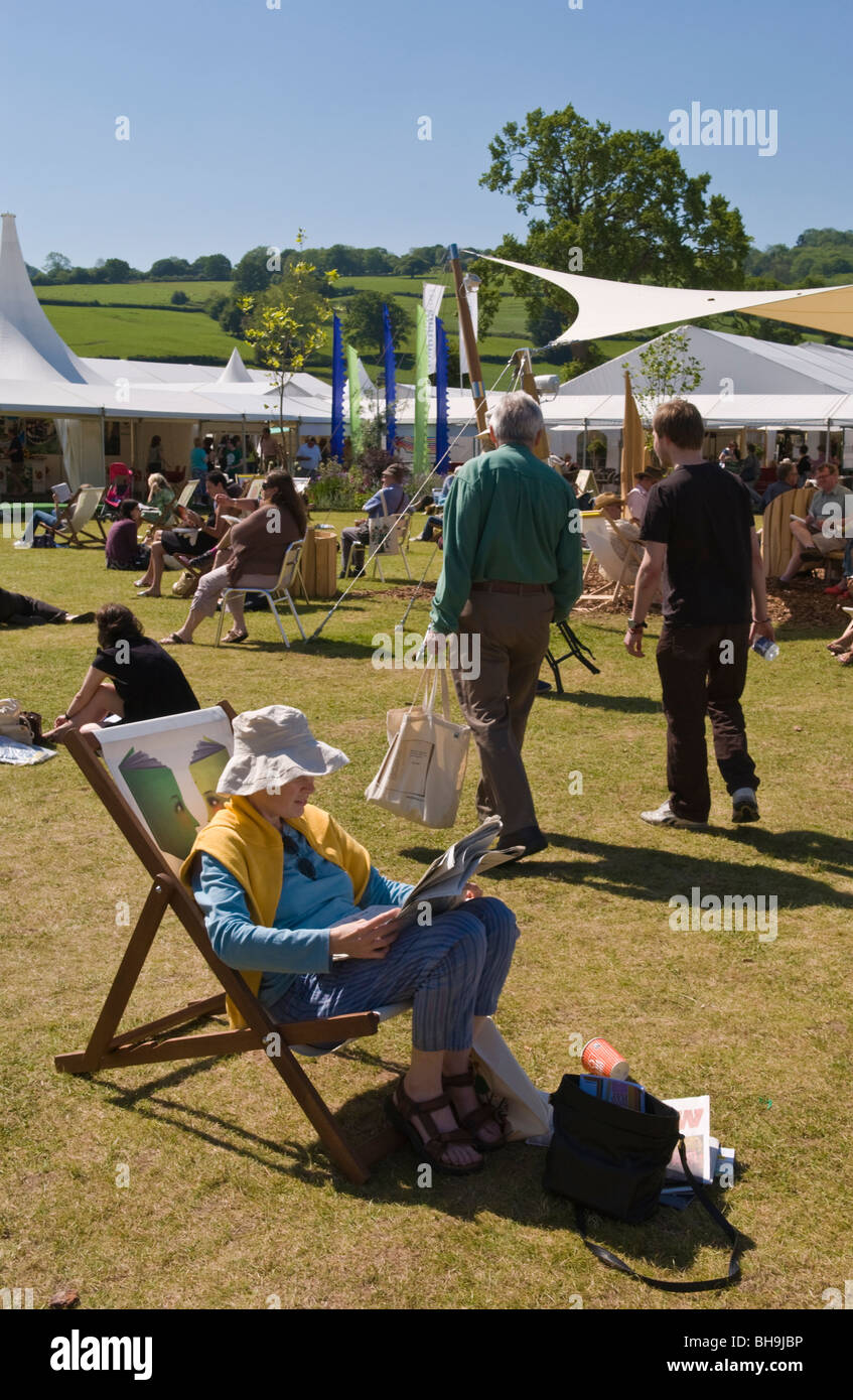 Senior woman wearing sun hat sat in deckchair reading newspaper and ...