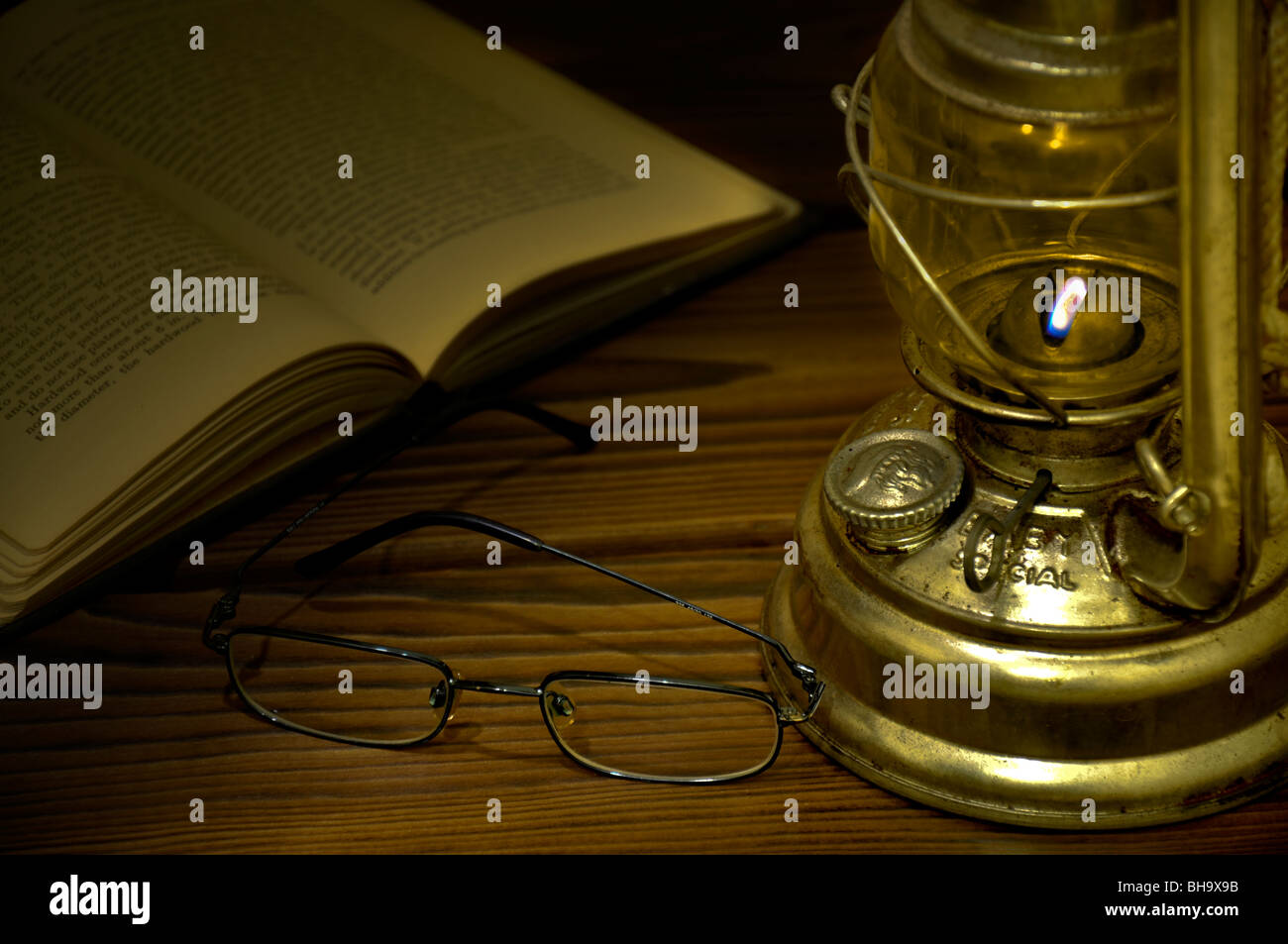 Cosy reading. Old book and glasses with vintage tilly lamp on a wooden ...