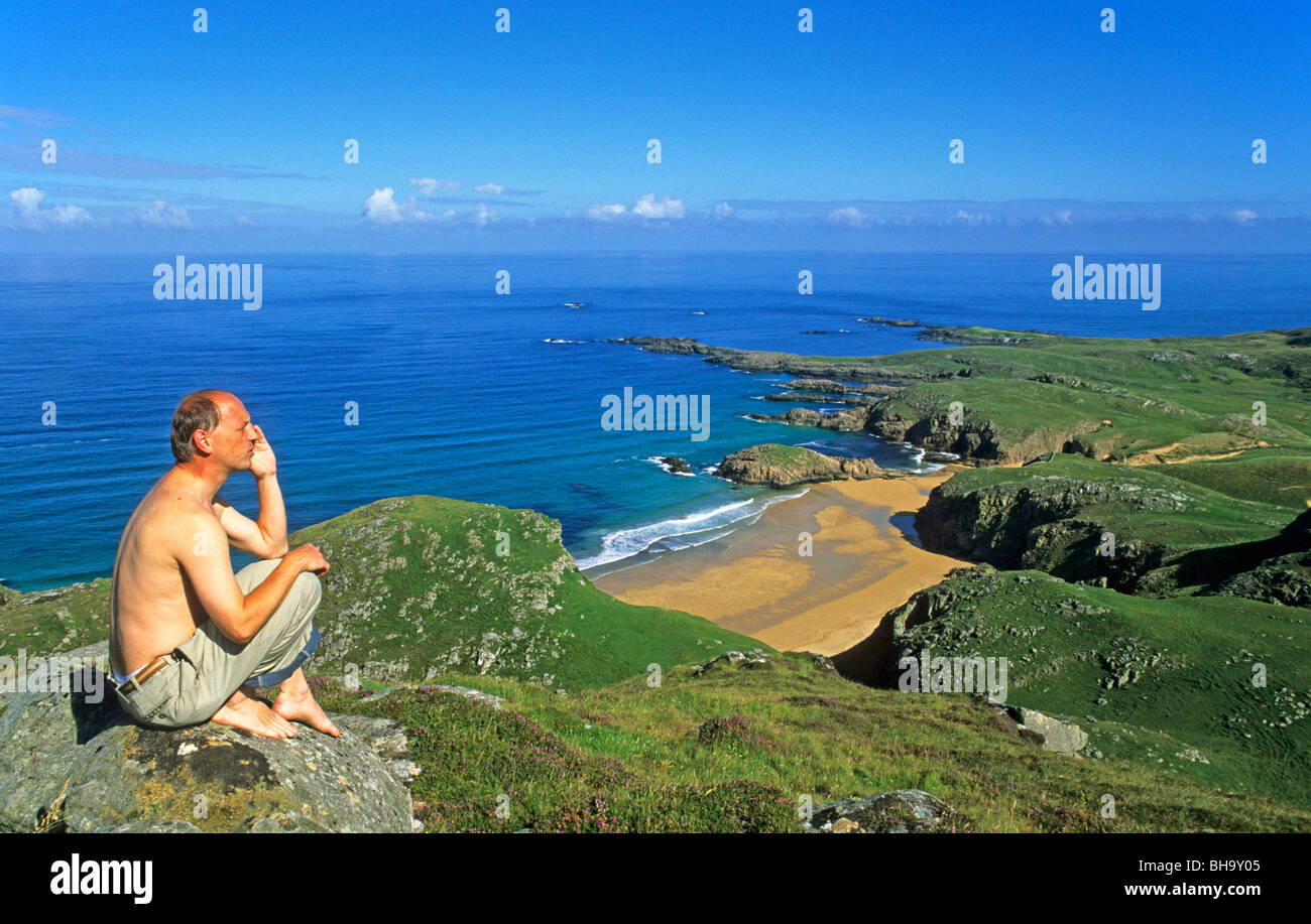 man sitting on a rock overlooking a beach near Melmore Head in County ...
