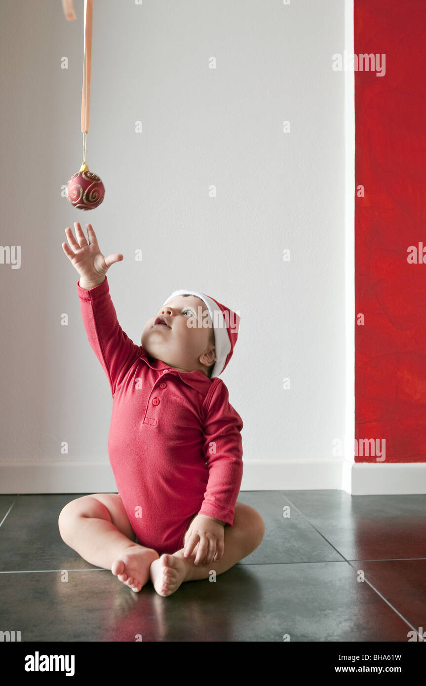 Baby boy sitting on floor reaching for Christmas ball Stock Photo - Alamy