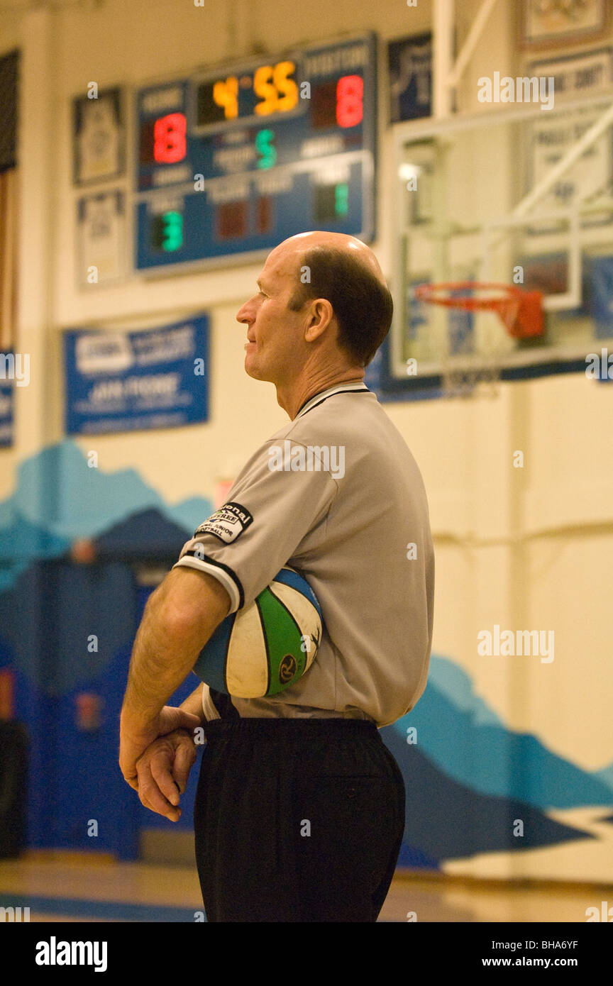 A referee at a girls 3rd grade basketball game with score board in ...