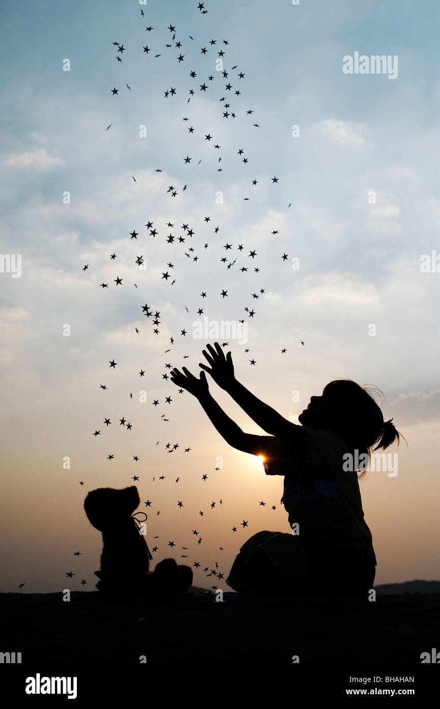 Silhouette of a young Indian girl catching falling stars at sunset ...