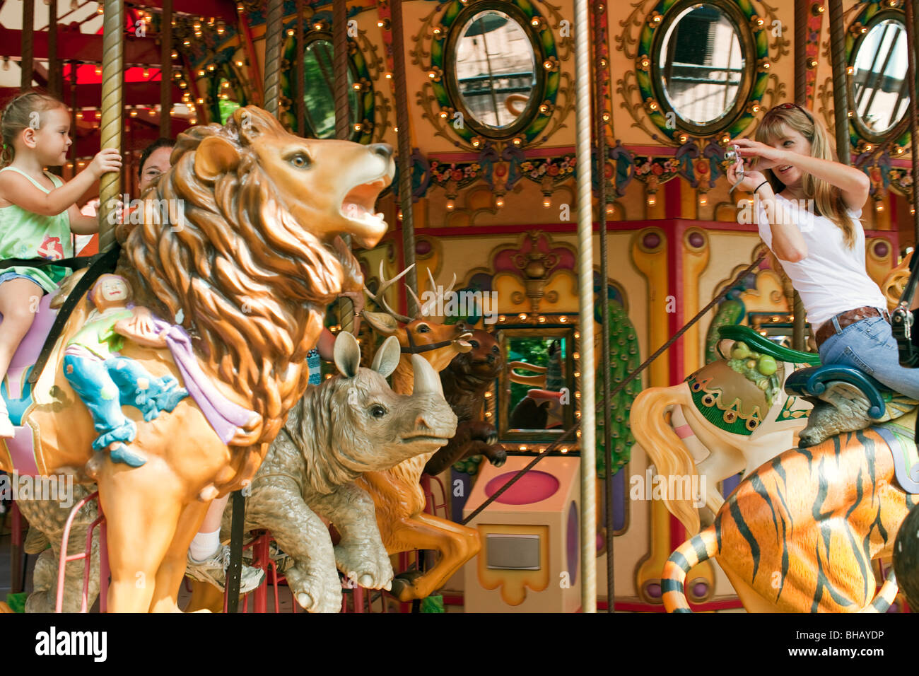 Young woman taking photo of little girl while riding carousel at ...