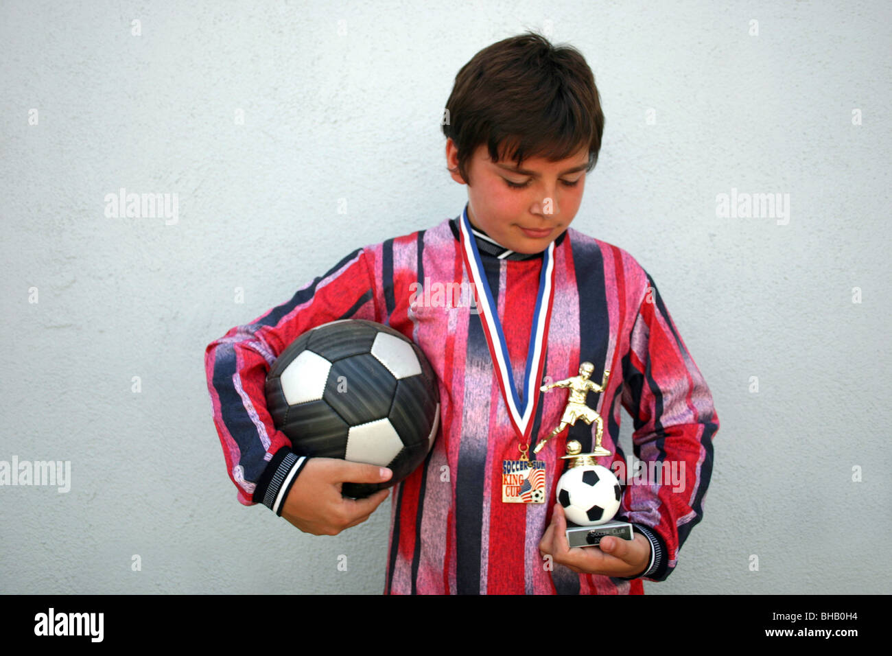 Young footballer looks down at his trophy while carrying a football ...