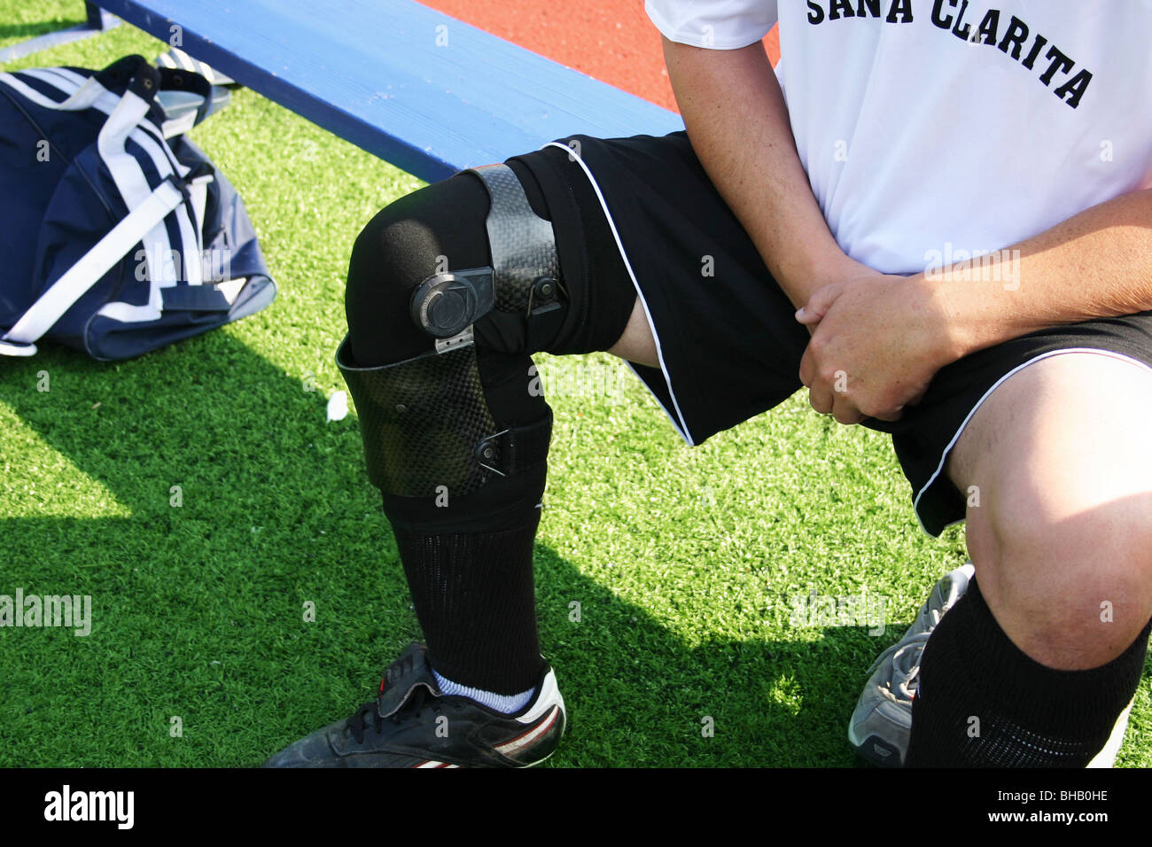 Footballer sits waiting on the bench after putting on his knee brace ...