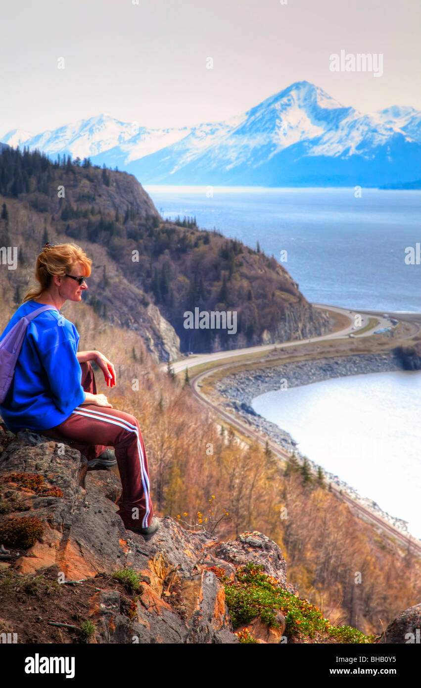 Woman sits on ridge overlooking Turnagain Arm with Seward Highway and ...